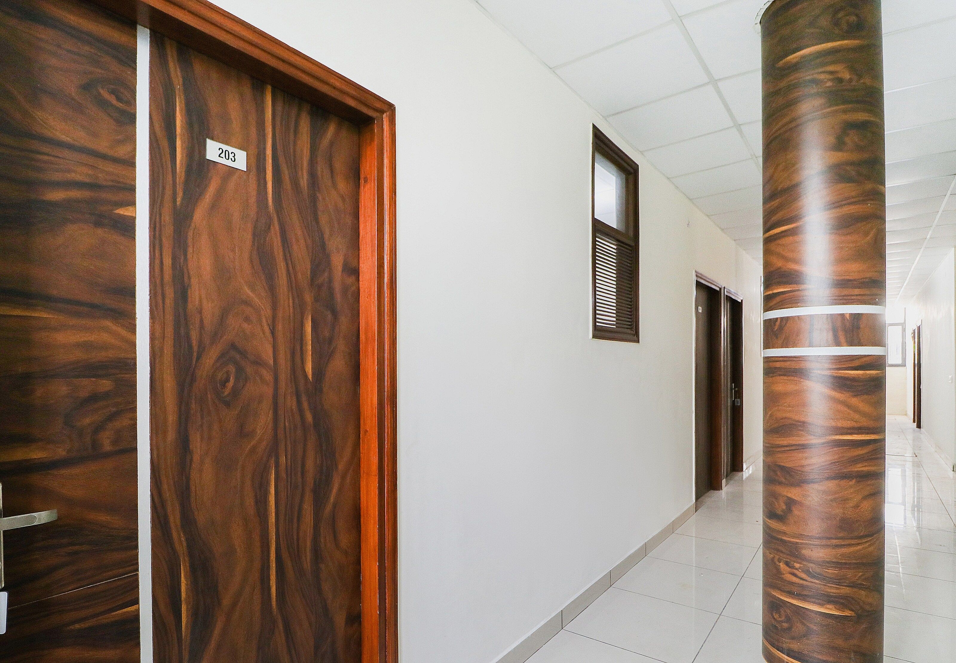 Corredor com portas de madeira, parede branca e um pilar com padrão que imita madeira.