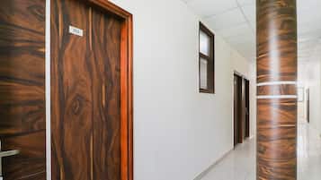 Corredor com portas de madeira, parede branca e um pilar com padrão que imita madeira.