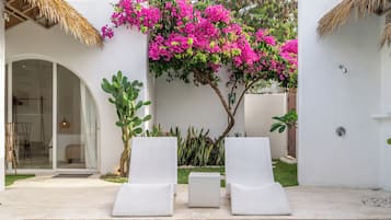 Área de piscina com duas cadeiras de descanso brancas, uma planta cacto e uma árvore florida.