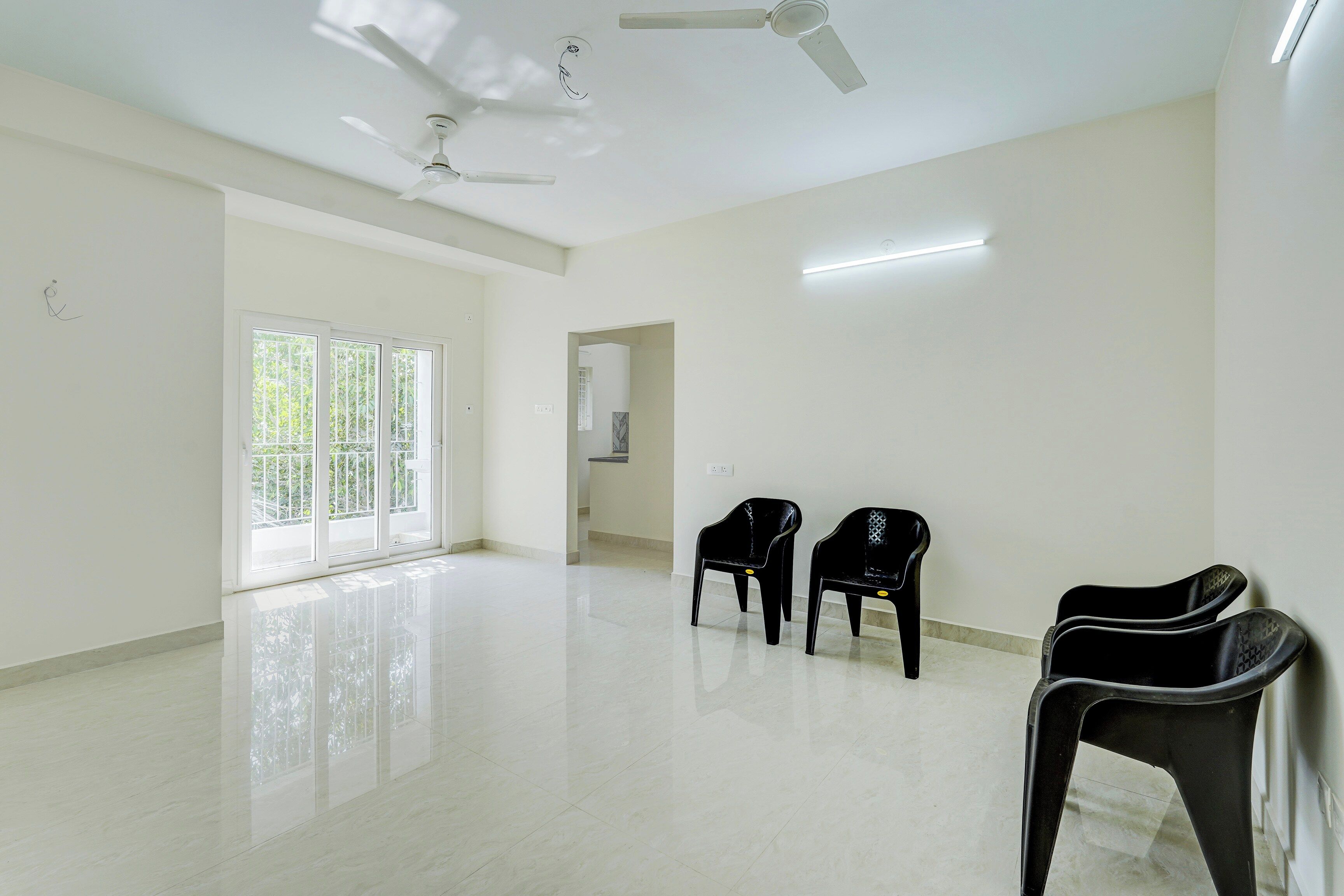 Um quarto espaçoso com pé direito alto, um ventilador de teto e duas cadeiras pretas.