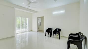 Um quarto espaçoso com pé direito alto, um ventilador de teto e duas cadeiras pretas.