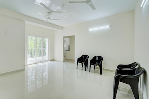 Um quarto espaçoso com pé direito alto, um ventilador de teto e duas cadeiras pretas.