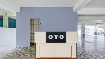 Um quarto com piso de azulejos, uma porta com grade de metal e uma placa com a palavra 'OYO' ao fundo branco.
