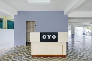 Um quarto com piso de azulejos, uma porta com grade de metal e uma placa com a palavra 'OYO' ao fundo branco.