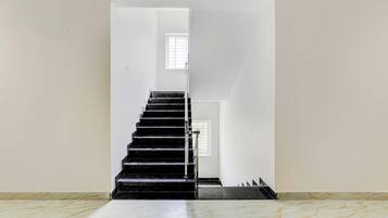 Uma escadaria com corrimão que leva a um patamar, uma janela com persianas e um piso de mármore.
