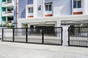 Um edifício residencial com vários andares e área de estacionamento fechada por portão.