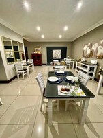 Uma área de refeições com mesa posta para quatro pessoas, rodeada por cadeiras brancas. Há um armário com um espelho e um quadro na parede.