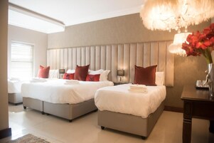 Quarto de hotel com duas camas, um encosto de cabeça grande e acolchoado, luminárias laterais e um abajur sobre uma mesa de cabeceira.