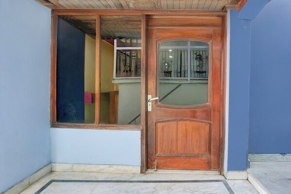 Uma porta de madeira com um painel de vidro e um portão de metal, dando acesso a um hall de entrada com azulejos.