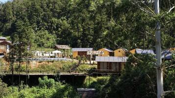 Paisagem rural com uma ponte de madeira, um edifício amarelo e uma colina arborizada.