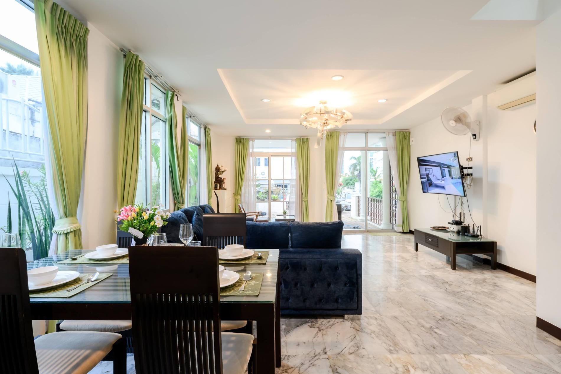 Uma sala de jantar moderna com piso de mármore, uma mesa posta para dois e um sofá azul escuro ao fundo.