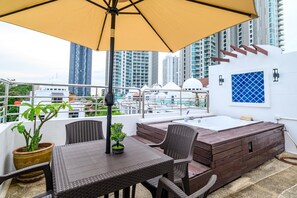 Terraço no telhado com mesa, cadeiras, banheira de hidromassagem e plantas em vasos.