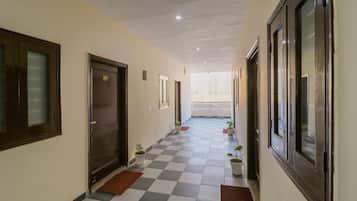 Um corredor com piso xadrez, portas com painéis de vidro e plantas em vasos.
