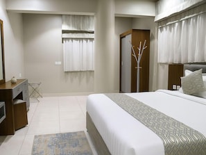 Quarto de hotel com cama, escrivaninha, cadeira, guarda-roupa e cabideiro.