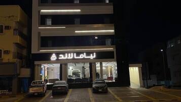 Um hotel com fachada moderna, vários andares e um estacionamento com carros.
