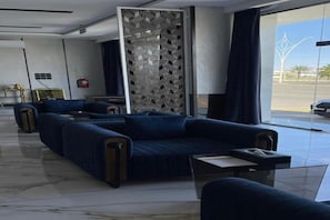 Um saguão de hotel com um sofá em formato de L, uma mesa pequena e um painel decorativo.