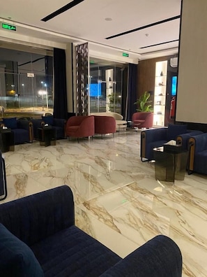 Um lobby moderno com áreas de estar, piso de mármore e divisória de vidro.