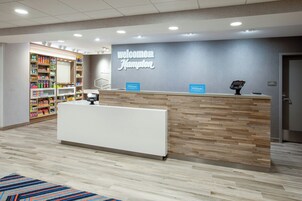 Bancada de recepção com um letreiro 'Welcome Hampton', um quiosque de autoatendimento e uma estante com lanches.