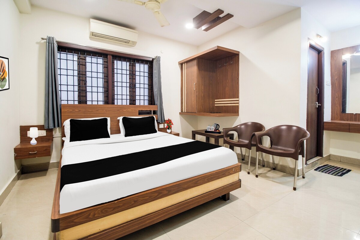 Quarto de hotel com uma cama grande, uma mesinha de cabeceira, uma cadeira, uma pequena mesa com cafeteira e um espelho.