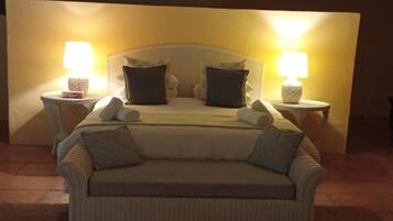 Quarto de hotel com cama, duas luminárias de cabeceira, um sofá e uma cabeceira.
