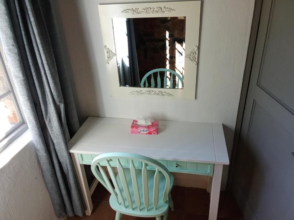 Quarto com escrivaninha branca, cadeira azul clara, espelho com detalhes decorativos e janela com cortinas.