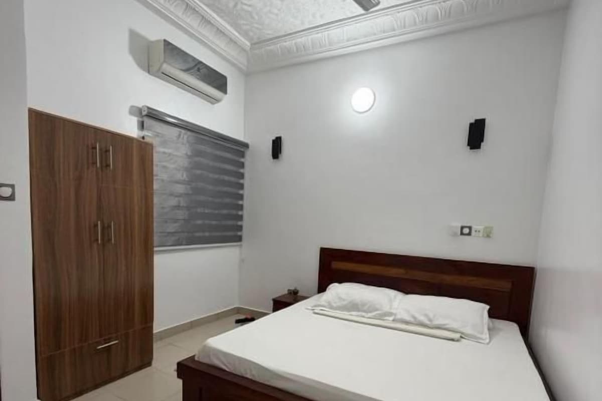 Quarto com cama, guarda-roupa, ventoinha no teto e ar condicionado fixado na parede.