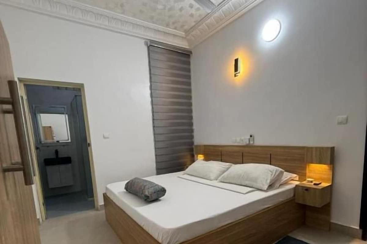 Quarto com cama, ventoinha no teto, mesa de cabeceira e luminária na parede.