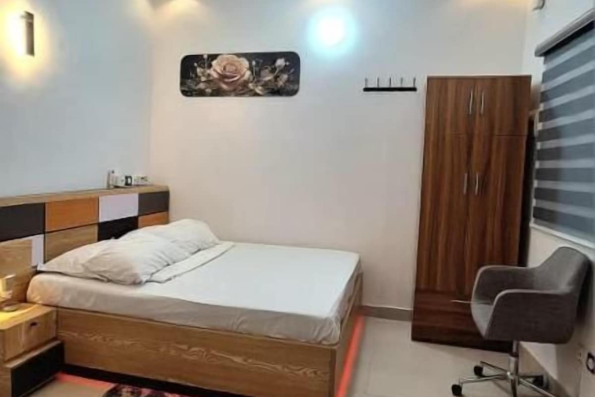 Quarto moderno com cama, mesa de cabeceira, criado-mudo, cadeira, guarda-roupa e ventilador de teto.