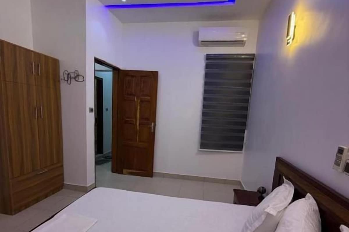 Quarto com cama, guarda-roupa, porta e janela.