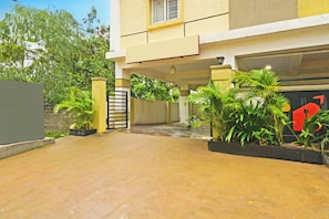 Edifício residencial com entrada por portão, calçada e vasos de plantas.
