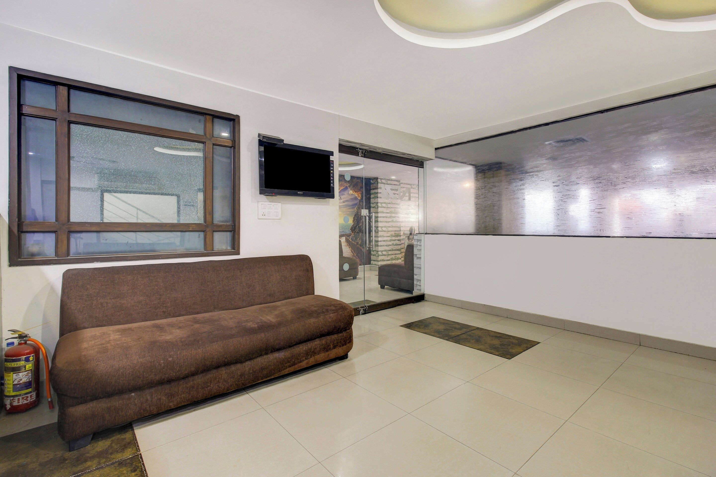 Quarto com sofá, televisão fixada na parede e extintor de incêndio no chão.