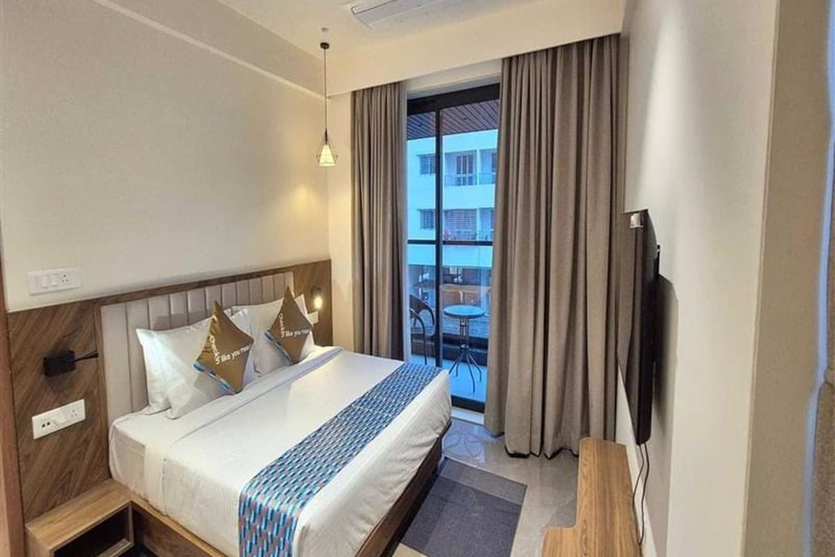Quarto de hotel com cama, televisão, janela com cortinas e varanda.