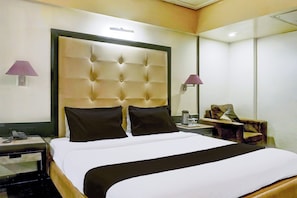 Quarto de hotel com uma cama grande, duas luminárias de cabeceira, uma cadeira e mesa de cabeceira com telefone.