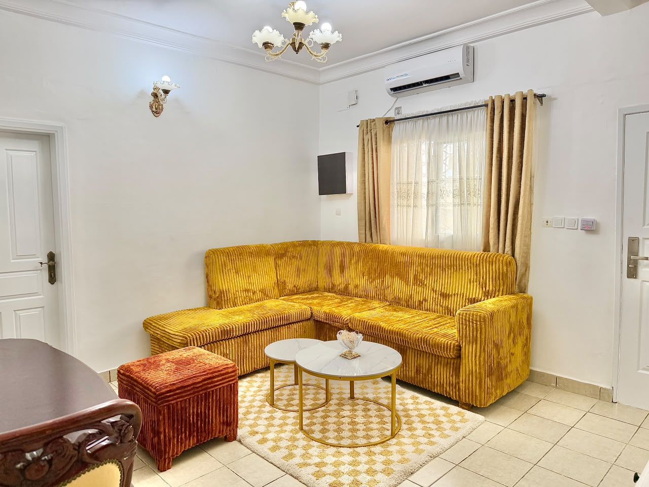 Sala de estar com sofá amarelo, mesa redonda pequena e um banquinho vermelho.