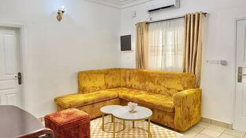 Sala de estar com sofá amarelo, mesa redonda pequena e um banquinho vermelho.