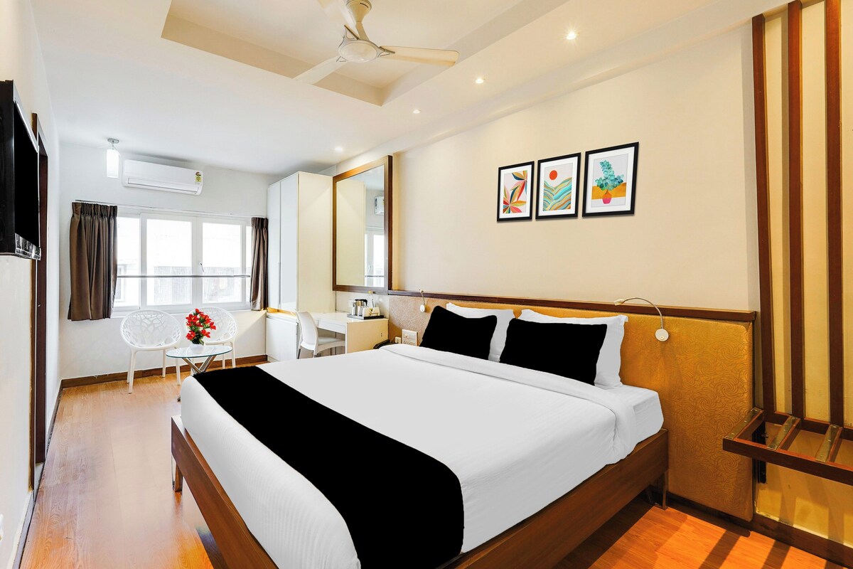 Quarto de hotel com cama, escrivaninha, cadeira, janela e parede com três quadros emoldurados.