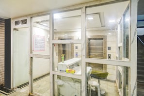 Um saguão de hotel com balcão de recepção, divisória de vidro e elevador.