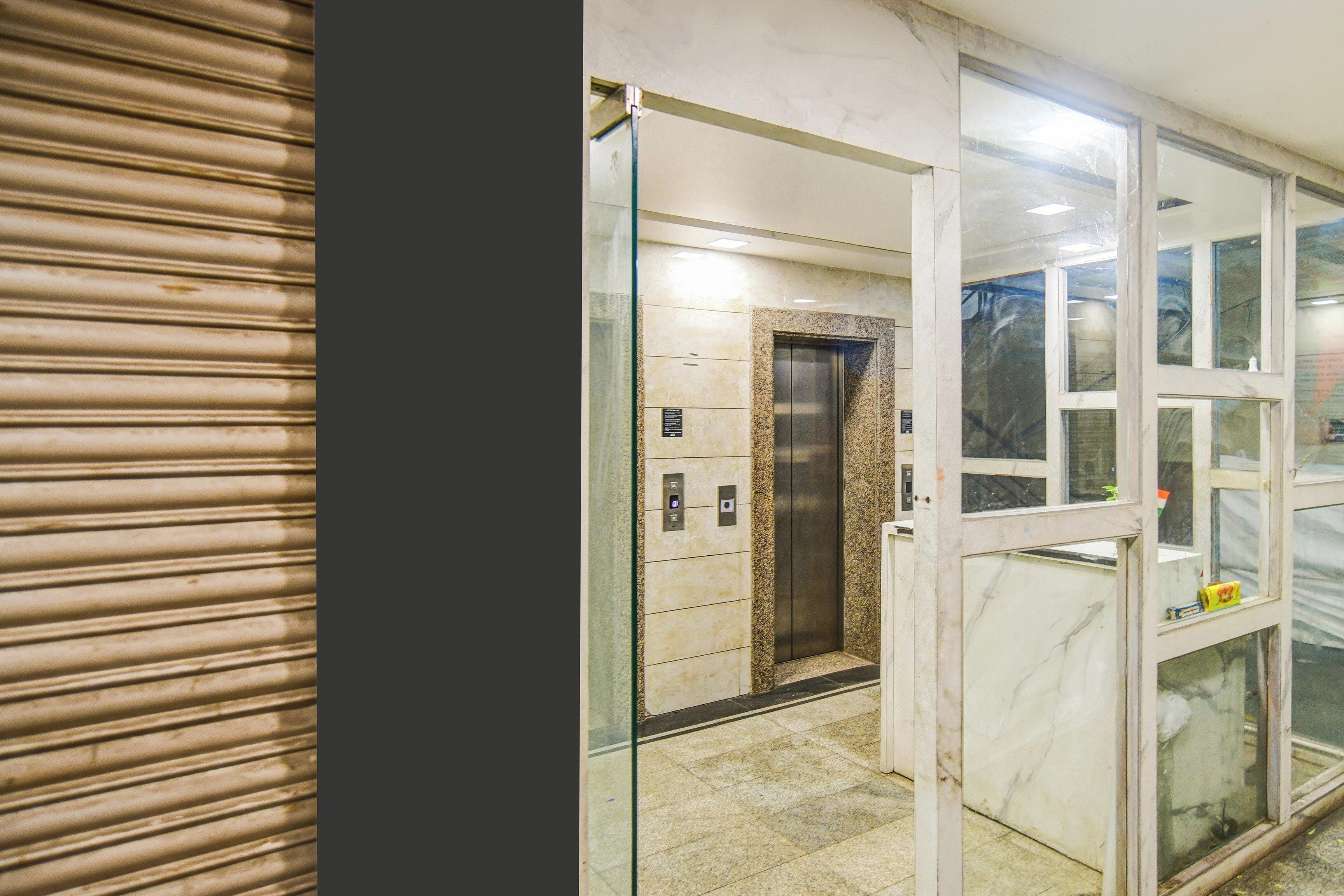 Um elevador com parede de mármore e porta de vidro, que dá acesso a um espaço com chão em azulejos.