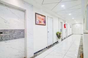 Um corredor limpo e moderno, com paredes de mármore, um quadro emoldurado, um extintor de incêndio e um vaso de plantas.