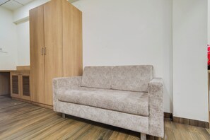 Quarto com guarda-roupa de madeira, sofá cinzento e chão de madeira.