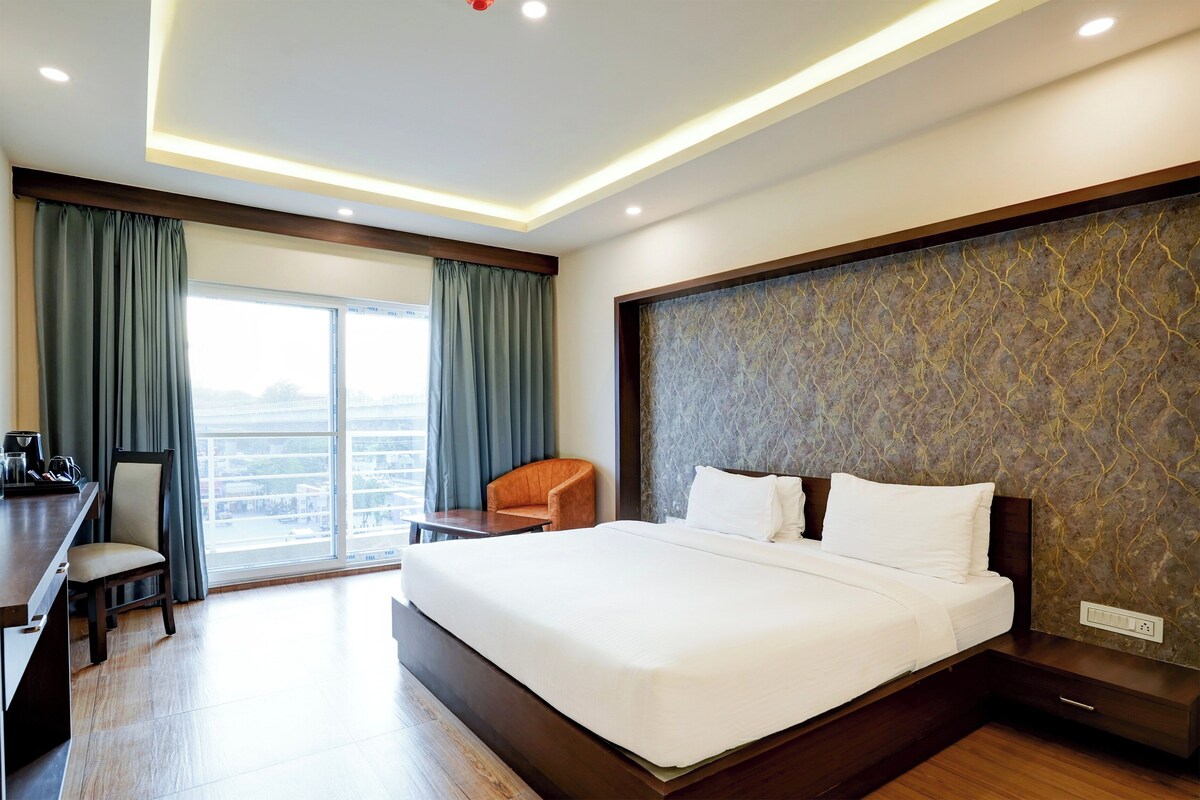 Quarto de hotel com cama grande, escrivaninha, cadeira e vista para a cidade pela janela.