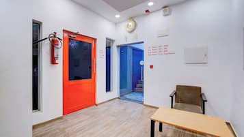 Corredor de hotel com uma porta vermelha, extintor de incêndio, mesa e uma cadeira.