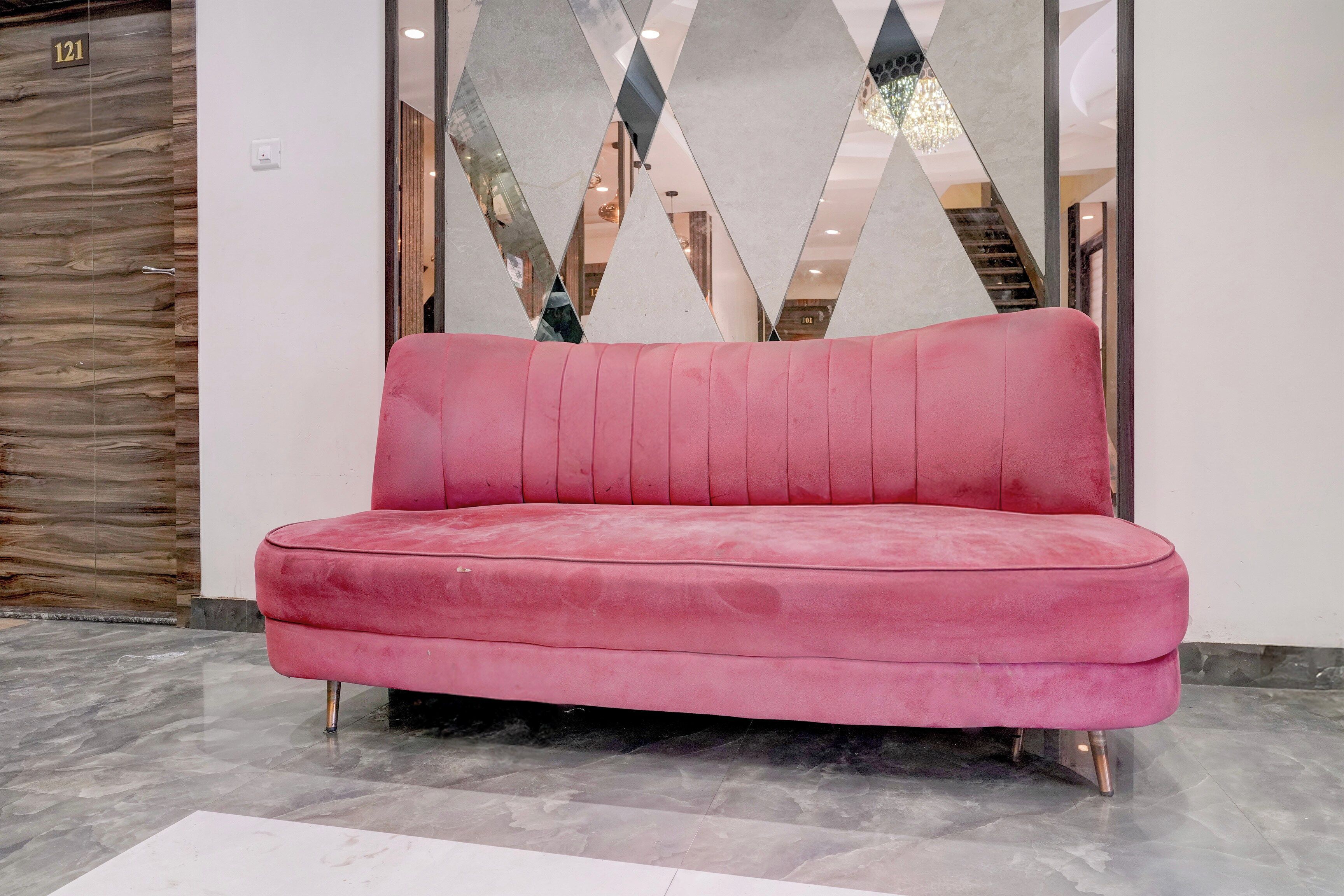 Um sofá rosa num lobby moderno com piso de mármore e divisória de vidro geométrica.