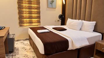 Quarto de hotel com cama, mesa de cabeceira e ventoinha na parede.
