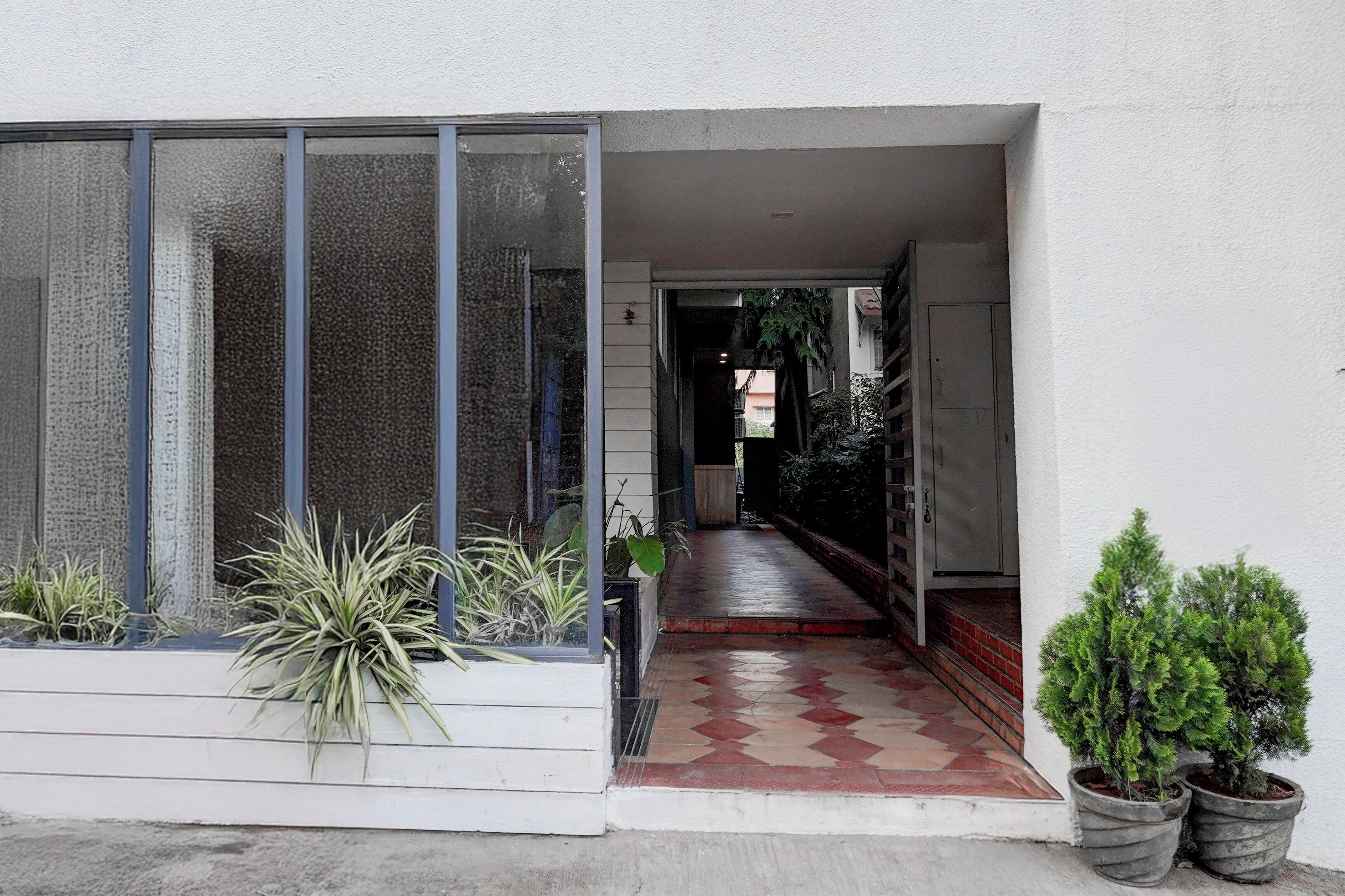 Entrada residencial com caminho de azulejos que leva à porta, plantas em vasos e janela com vista para a rua.