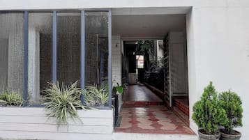 Entrada residencial com caminho de azulejos que leva à porta, plantas em vasos e janela com vista para a rua.
