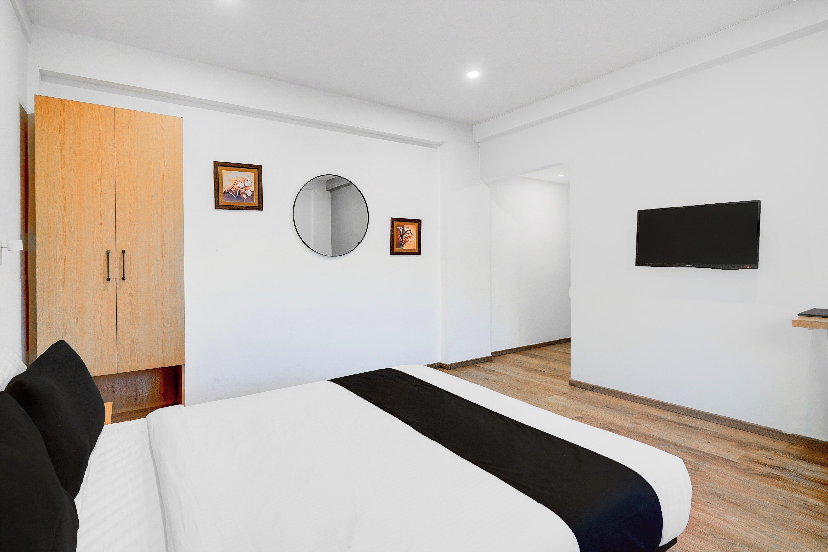 Quarto moderno com cama, guarda-roupa, espelho redondo e televisão na parede.