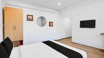 Quarto moderno com cama, guarda-roupa, espelho redondo e televisão na parede.