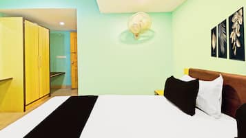 Quarto de hotel com cama, mesa de cabeceira, ventoinha na parede e porta para o banheiro.