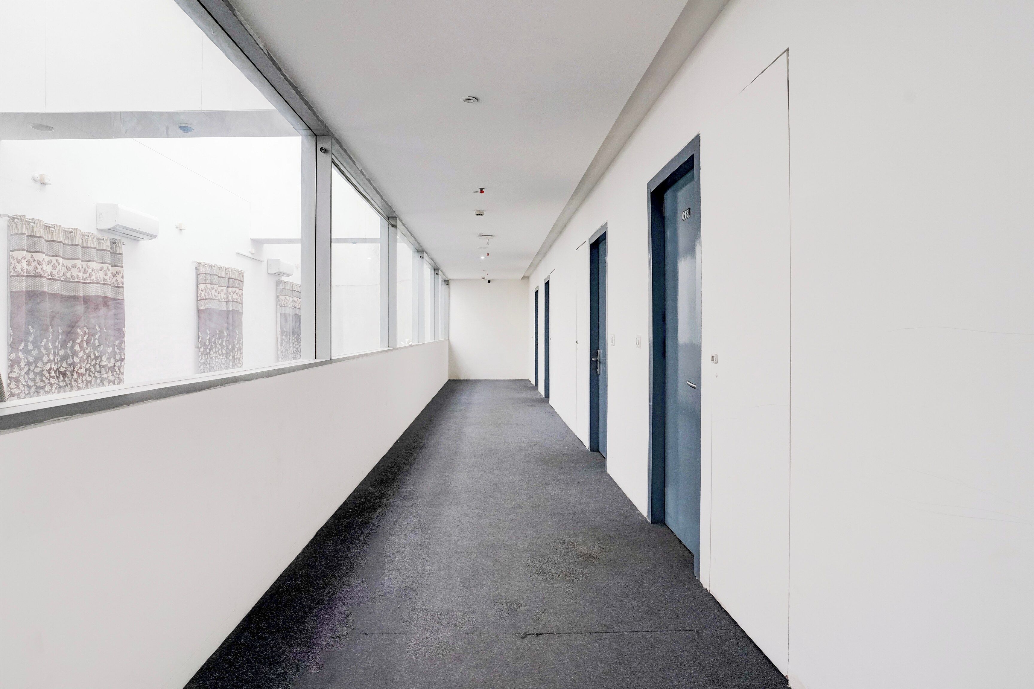 Um corredor longo e estreito com piso preto, paredes brancas e uma série de portas de um lado.